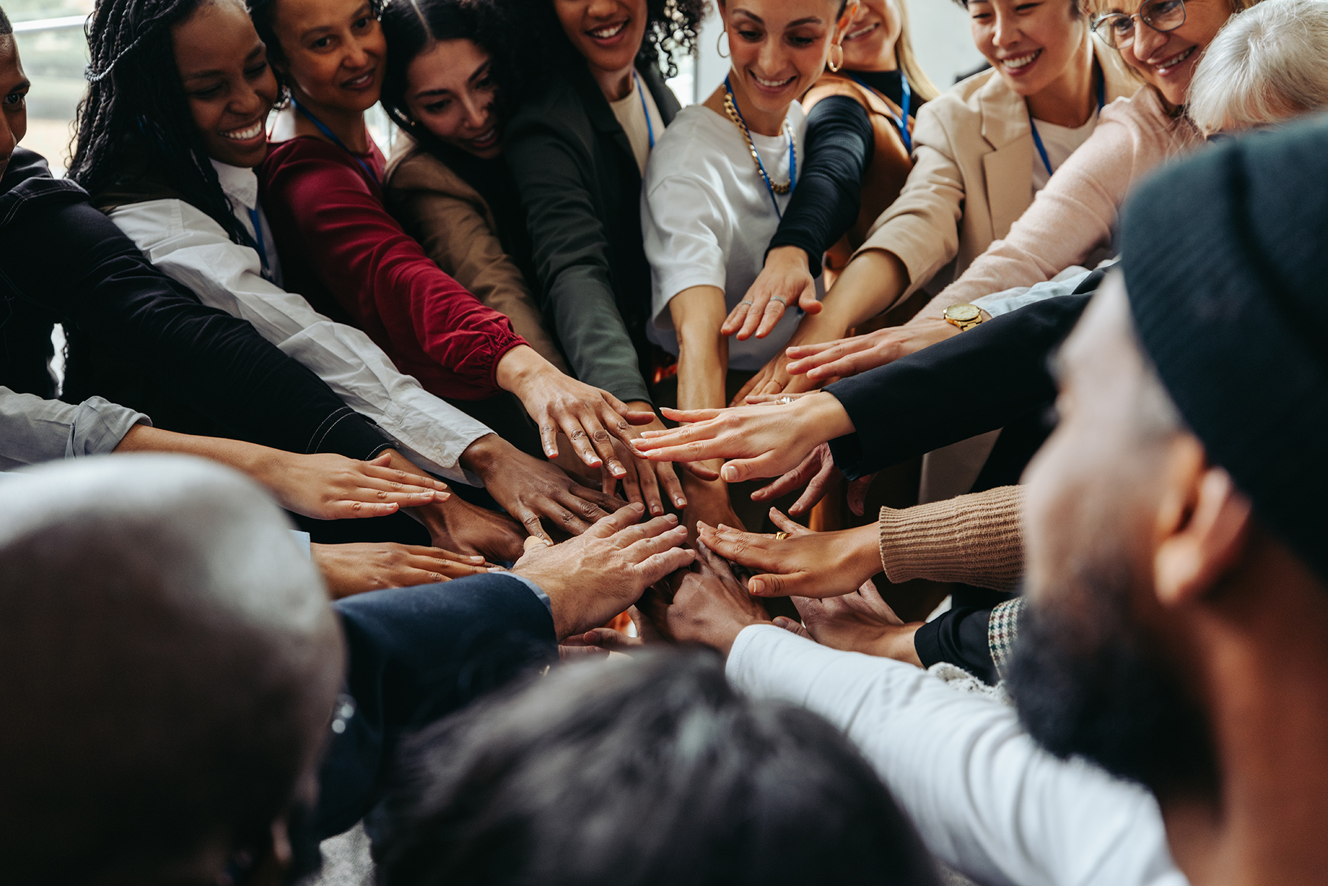Diverse coworkers putting hands in for a unified team huddle at work ...